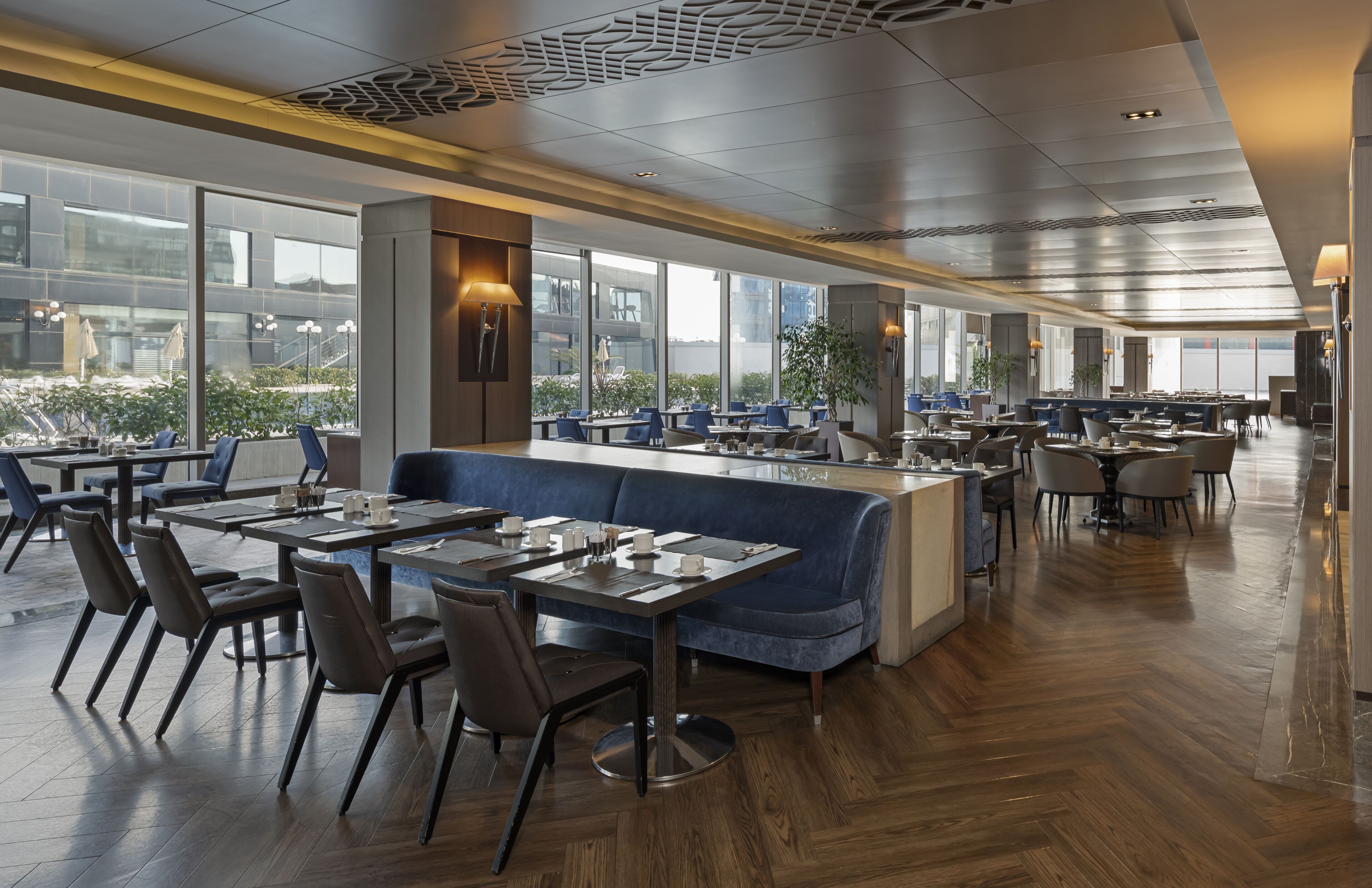 Um restaurante moderno com área de bar central, várias mesas de jantar e vista para a cidade através de grandes janelas.