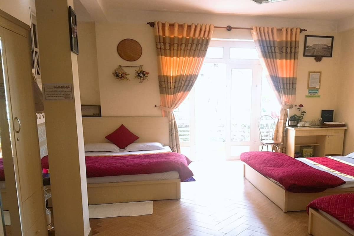 Quarto de hotel com duas camas, uma secretária e uma cadeira. Há uma janela com cortinas, uma porta e uma parede com um quadro emoldurado.