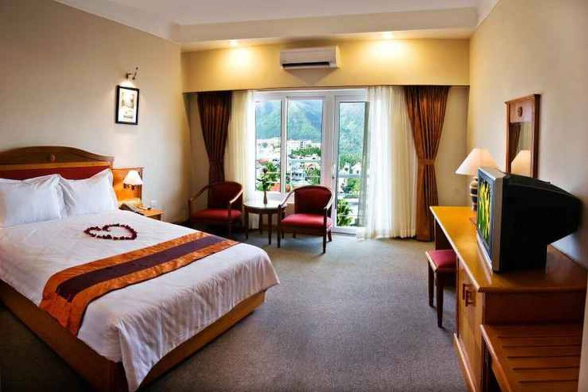 Quarto de hotel com uma cama grande, uma escrivaninha com televisão, uma cadeira e vista para uma paisagem montanhosa pela janela.