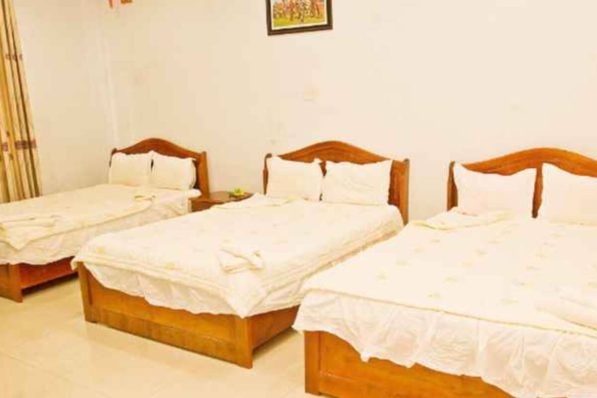 Quarto de hotel com três camas de madeira, cada uma com roupa de cama branca.