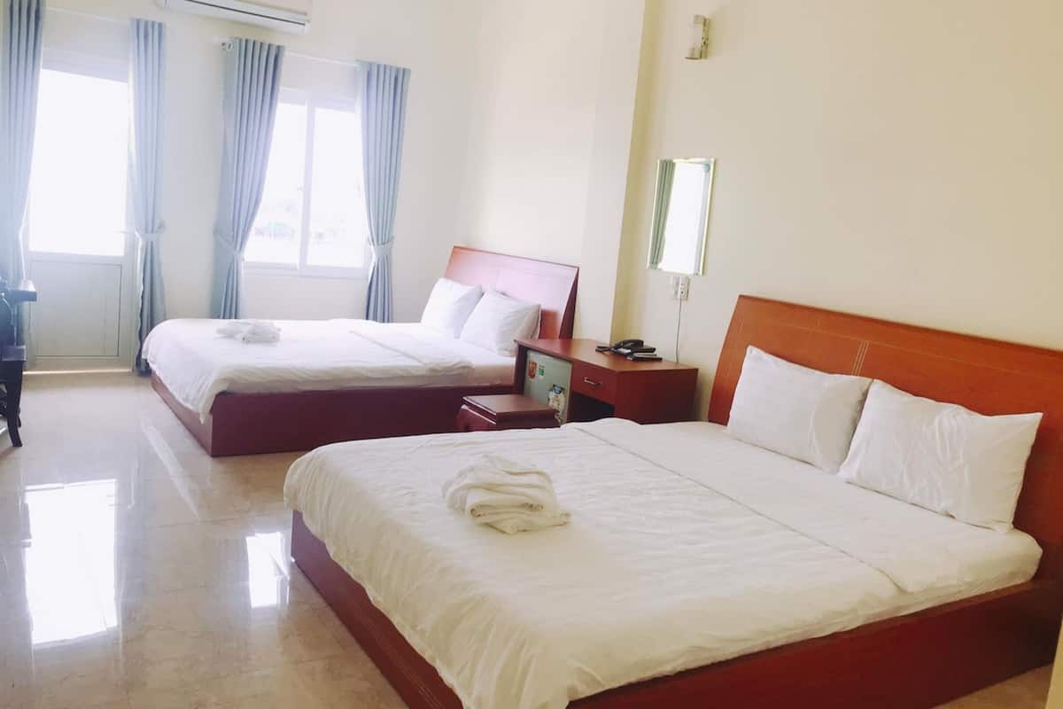 Quarto de hotel com duas camas, uma escrivaninha, uma cadeira e uma janela com cortinas.