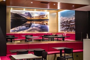 Restaurante com assentos em vermelho, mesas e murais panorâmicos nas paredes, com design de interiores moderno.