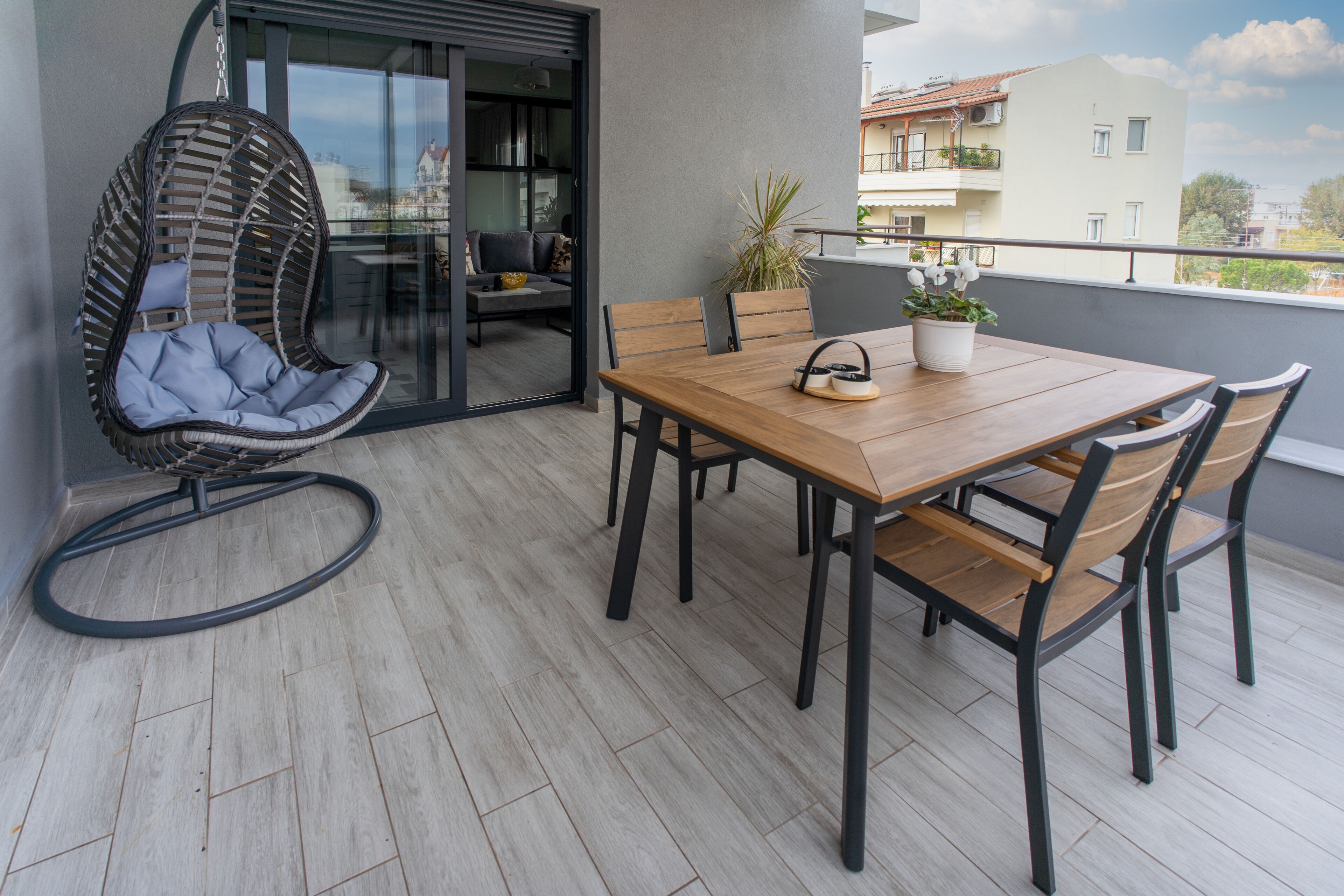 Uma varanda com mesa e cadeiras de madeira, uma cadeira suspensa e um vaso com planta.