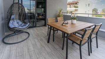 Uma varanda com mesa e cadeiras de madeira, uma cadeira suspensa e um vaso com planta.