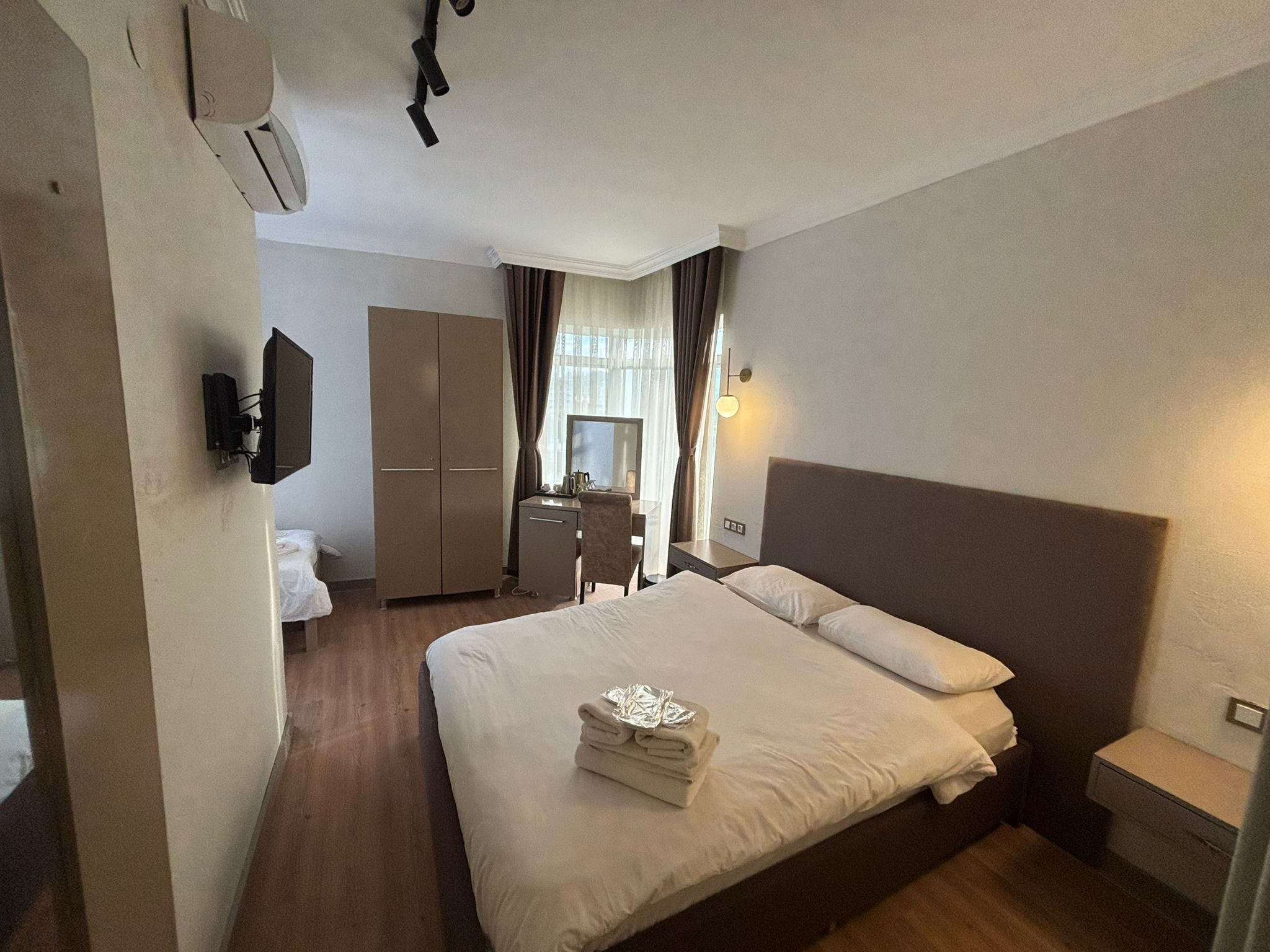 Quarto de hotel com uma cama grande, uma mesa, um guarda-roupa e uma televisão.