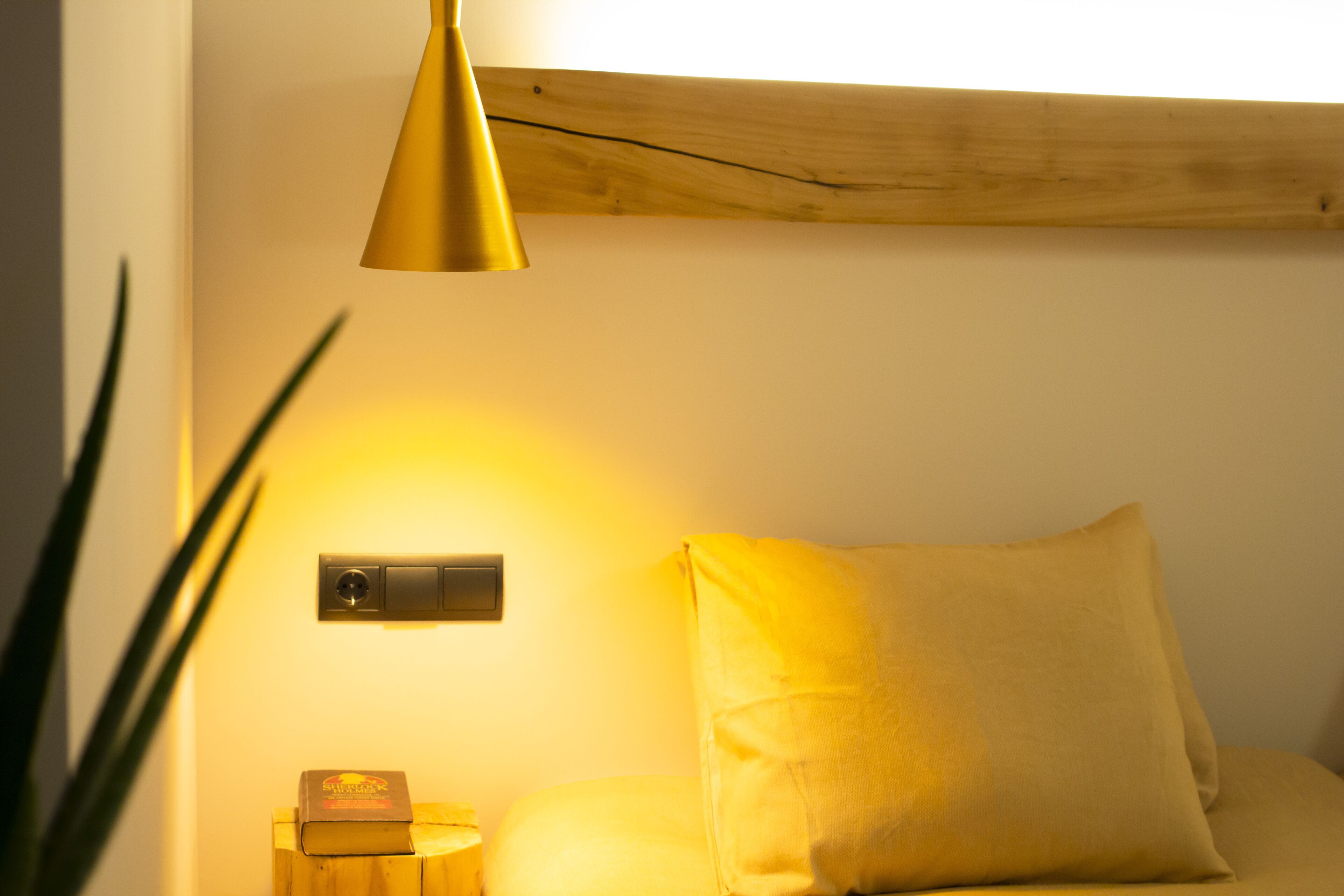 Quarto com cabeceira de madeira, mesa de cabeceira com abajur e cama com travesseiro.