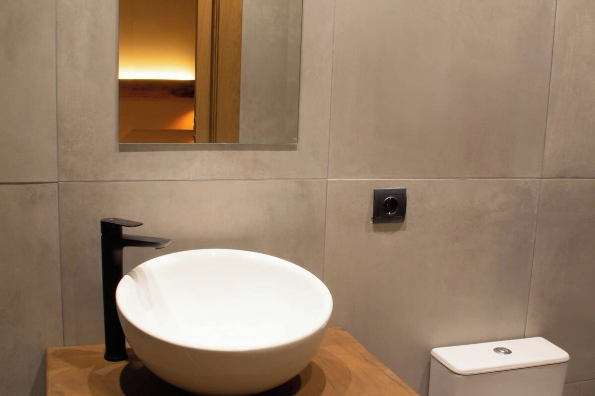 Casa de banho moderna com lavatório branco grande, torneira preta e sanita branca pequena.