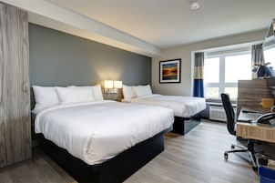 Quarto de hotel com duas camas, uma escrivaninha com cadeira, uma janela com cortinas e um quadro na parede.