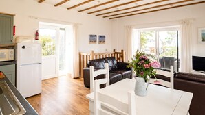 Uma sala ampla com teto de madeira, mesa de jantar com cadeiras, sofá de couro preto, cozinha com geladeira e micro-ondas, e varanda com vista.