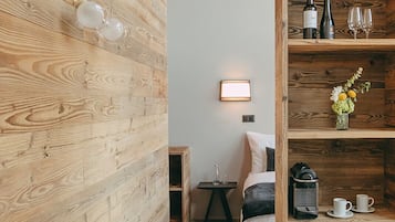 Interior em madeira com cama, mesa de cabeceira e uma estante com garrafas de vinho e copos.