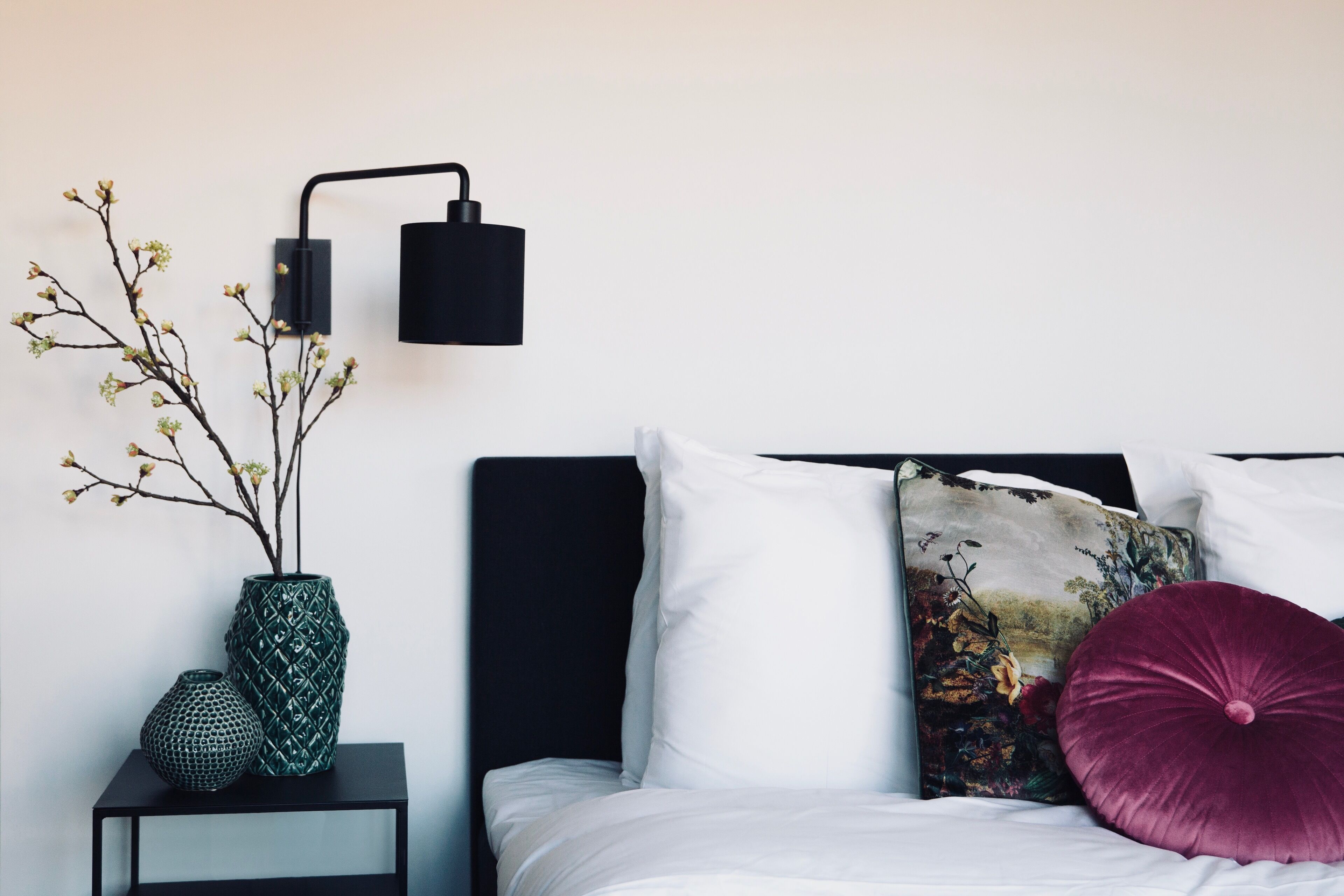 Cama bem arrumada com roupa de cama branca, cabeceira preta e almofadas decorativas.
