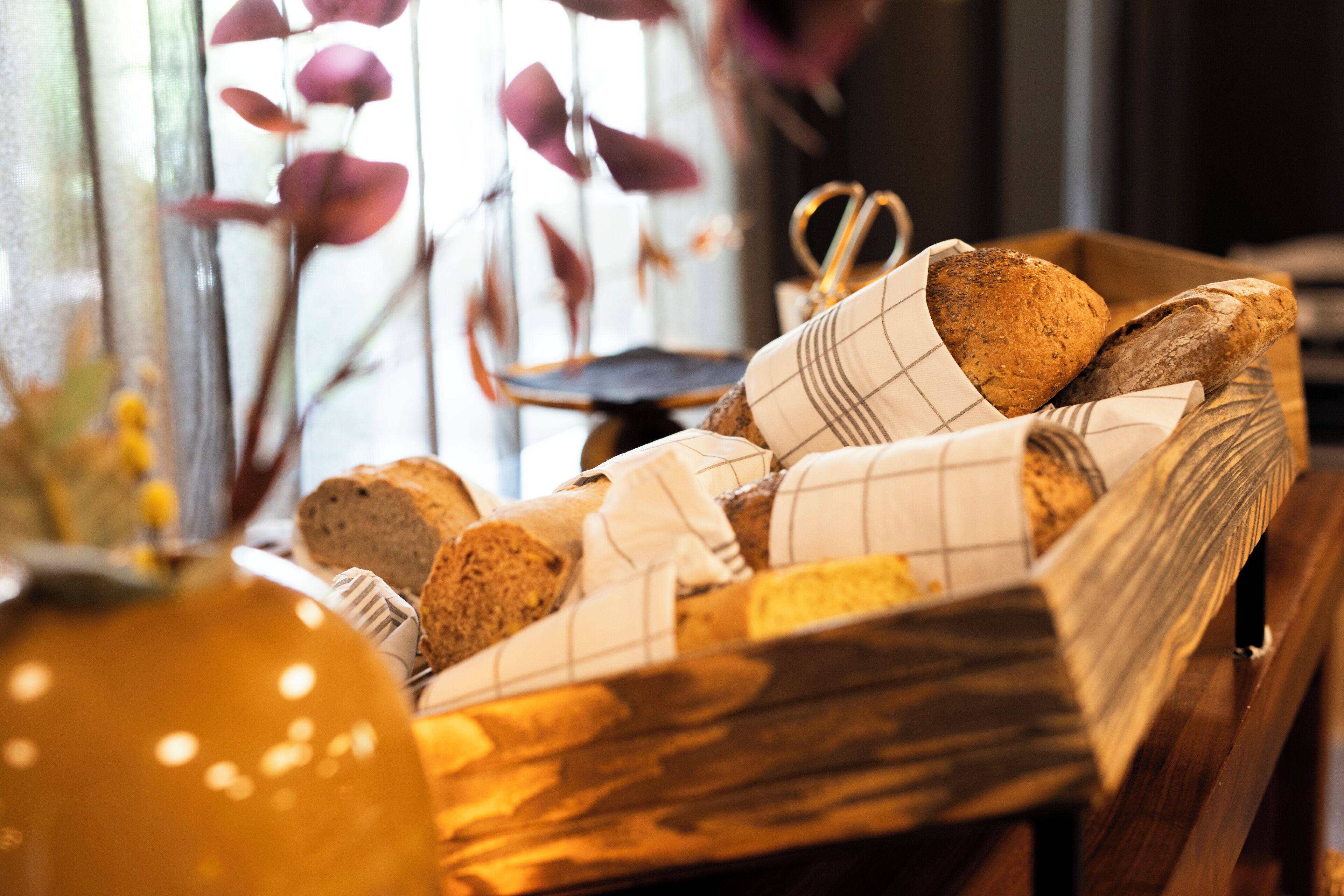 Cesta de madeira com diferentes tipos de pão, colocada sobre uma mesa de madeira.