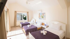 Quarto de hotel com duas camas, um ventilador de teto, janela com cortinas e um quadro na parede.