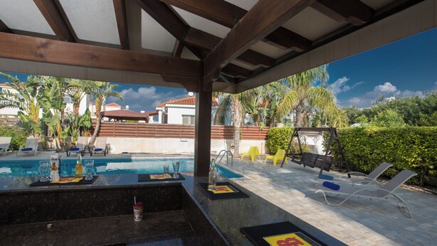 Área junto à piscina com bar, espreguiçadeiras e vista para um bairro residencial.