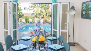 Uma área de jantar com vista para uma piscina, mesa posta com pratos, copos e um vaso de flores.