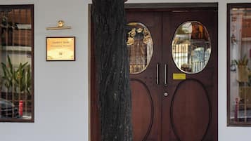 Uma entrada de prédio com porta de madeira, uma placa e uma árvore.
