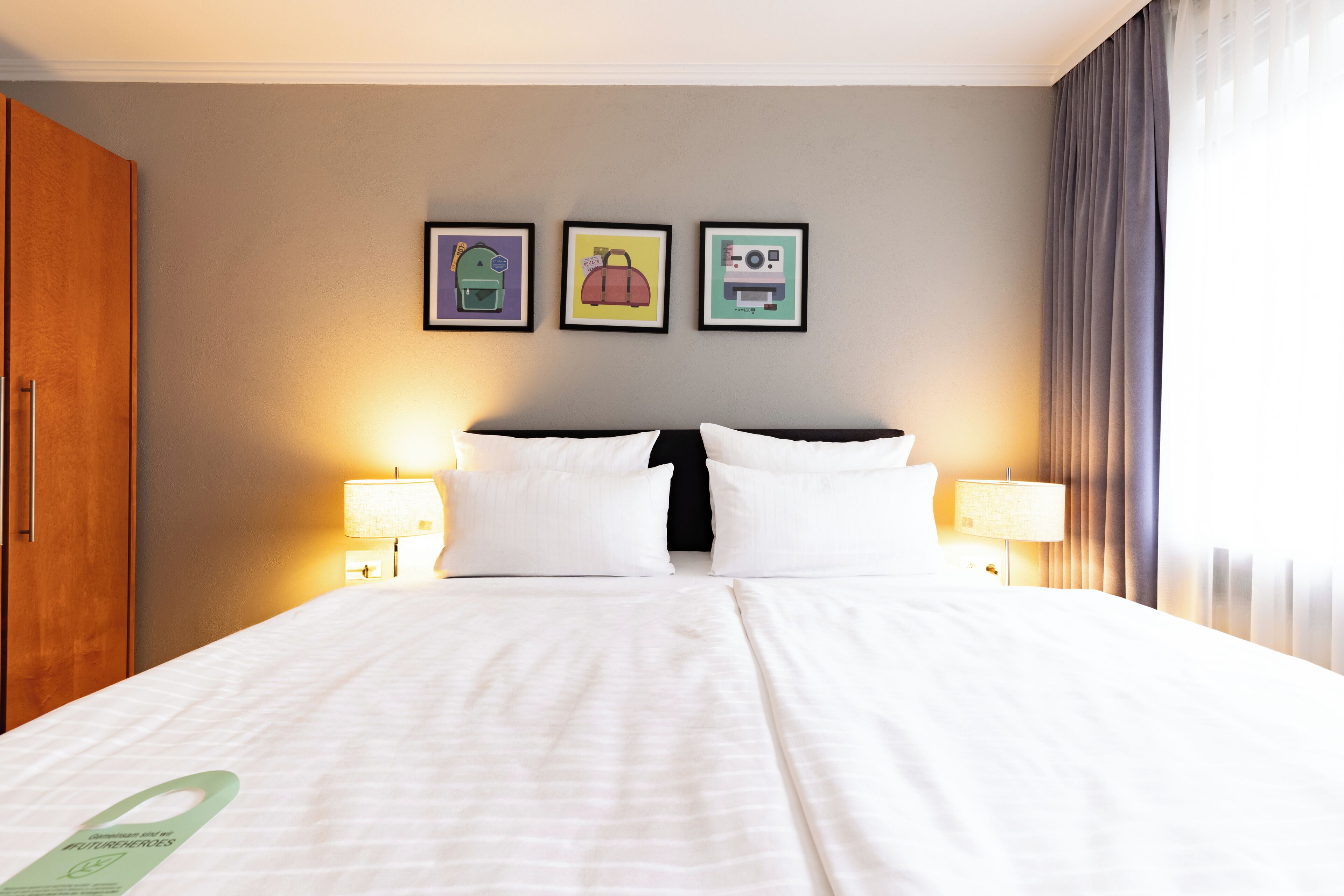 Quarto de hotel com uma cama grande, duas luminárias de cabeceira, um guarda-roupa e três quadros na parede.