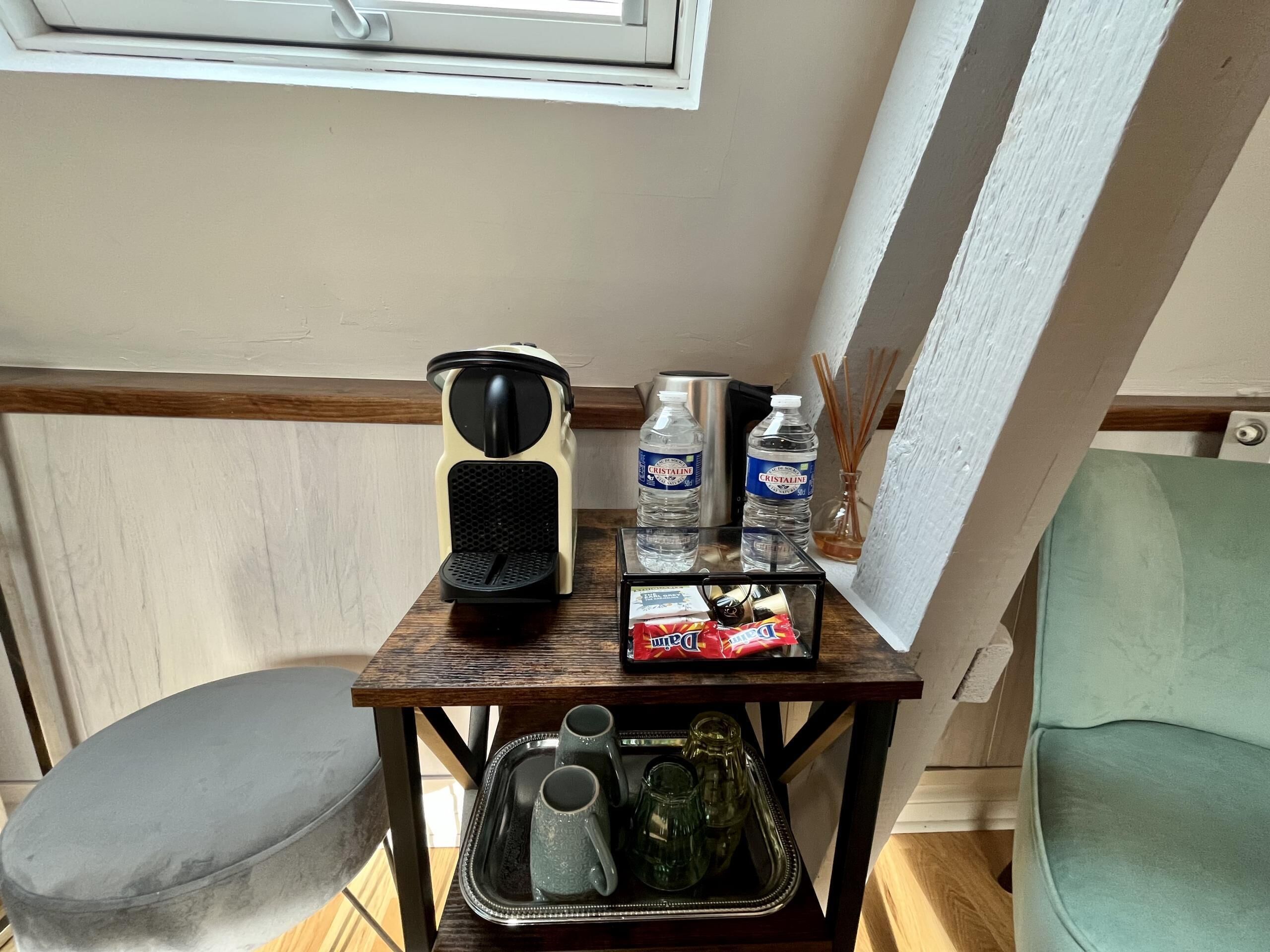 Uma pequena mesa com uma cafeteira, garrafas de água, um difusor e uma bandeja com chávenas e copos.