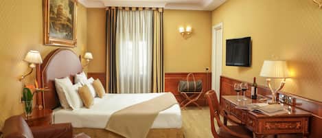 Quarto de hotel com cama, escrivaninha e cadeira, televisão e um quadro na parede.