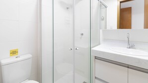 Uma casa de banho moderna com cabine de duche em vidro, lavatório branco e espelho sobre o lavatório.