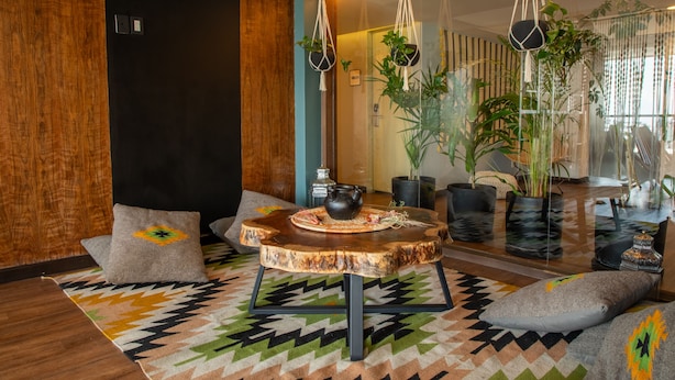Uma sala de estar moderna com uma mesa de centro redonda de madeira, dois vasos de macramé pendurados e um tapete estampado.