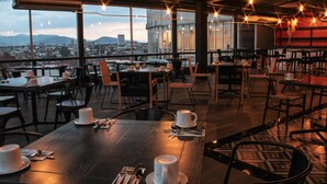 Restaurante com mesas preparadas para refeições, amplas janelas com vista para a cidade e decoração de interiores moderna.