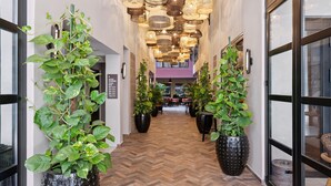 Um corredor com piso em padrão herringbone, grandes vasos de plantas e várias luminárias pendentes.
