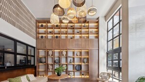 Um interior moderno com uma estante de madeira exibindo diversos objetos decorativos, uma mesa de madeira redonda com uma planta e cadeiras de vime.
