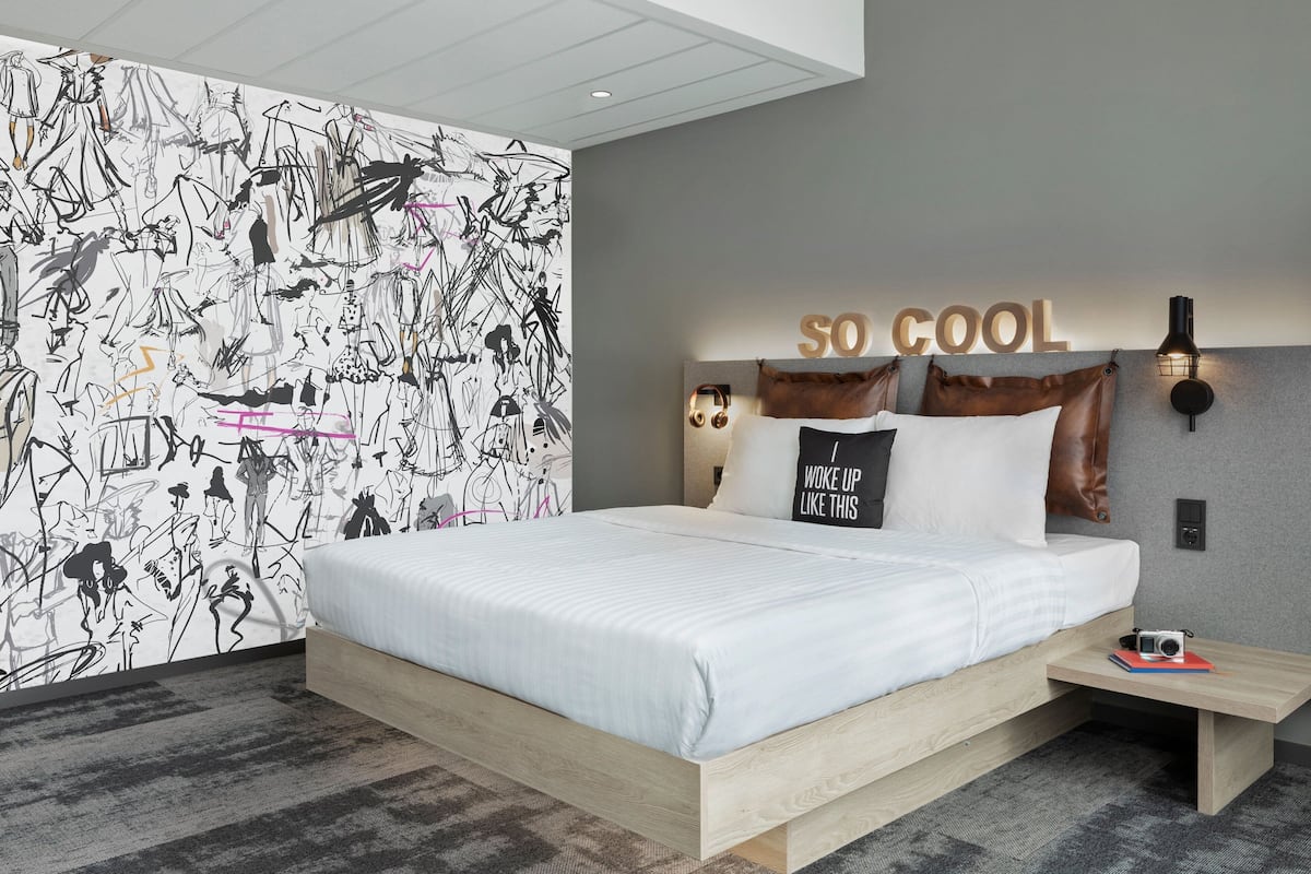 Um quarto moderno com uma cama grande, um mural na parede e um letreiro com a frase 'SO COOL' sobre a cama.