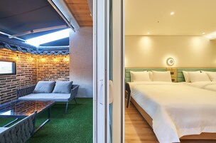 Quarto de hotel moderno com parede de tijolos, área com grama sintética verde, mesa de vidro e cama com roupa de cama branca.