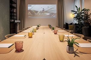 Uma sala de conferências com uma mesa comprida, cadeiras e uma tela exibindo uma apresentação.