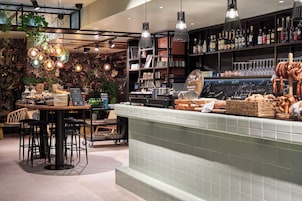 Uma área de bar com balcão exibindo petiscos e bebidas, prateleiras com garrafas e luminárias pendentes.