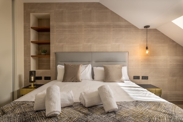 Quarto de hotel moderno com uma cama grande, uma estante embutida e um claraboia.