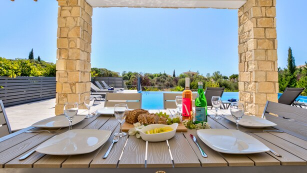 Mesa de jantar posta para dois, com vista para uma piscina e vegetação.