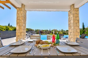 Mesa de jantar posta para dois, com vista para uma piscina e vegetação.