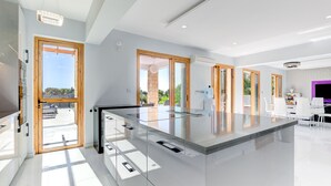 Uma cozinha moderna com uma ilha grande, eletrodomésticos embutidos e grandes janelas com vista para o exterior.