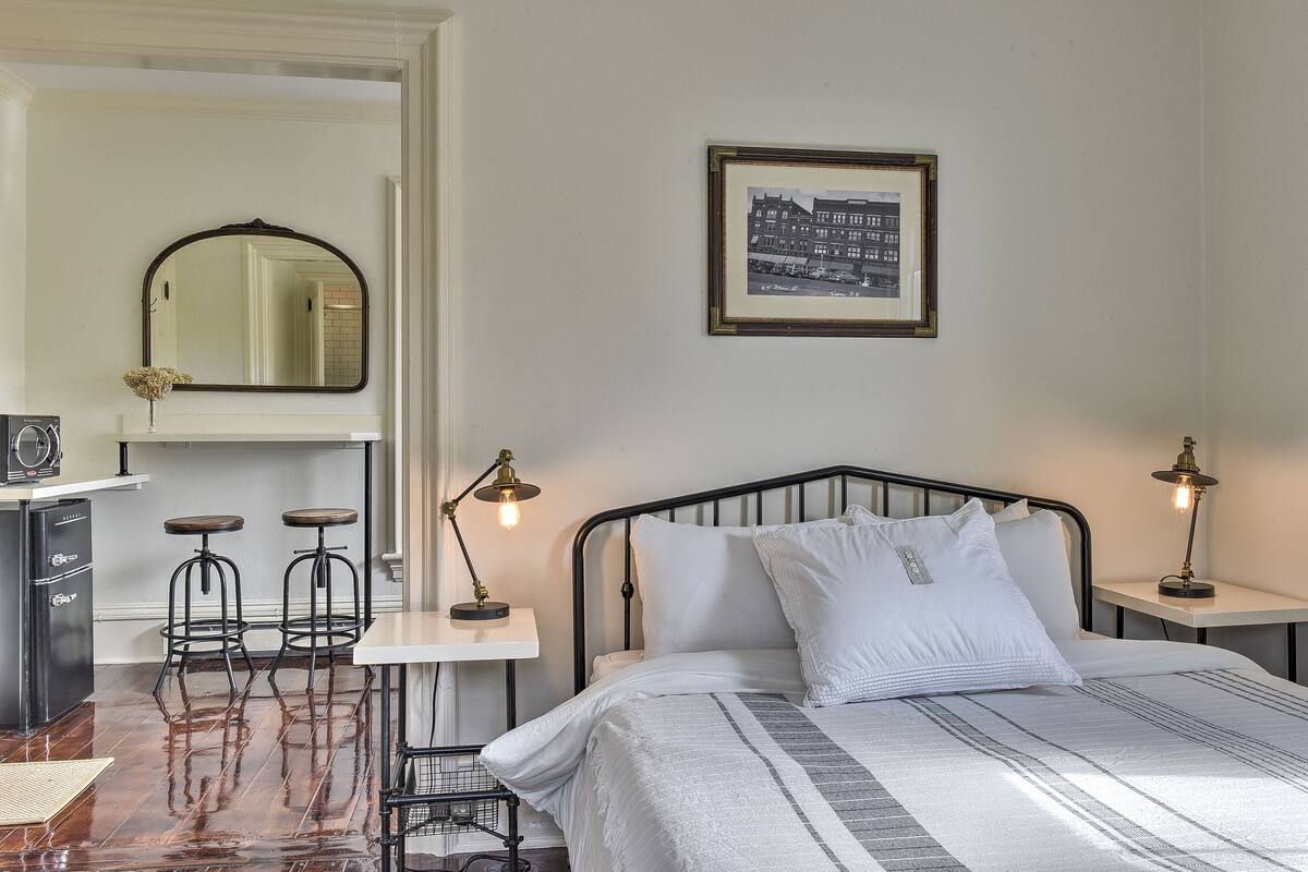 Um quarto com uma cama, duas mesas de cabeceira com luminárias, uma escrivaninha com cadeira e um espelho.