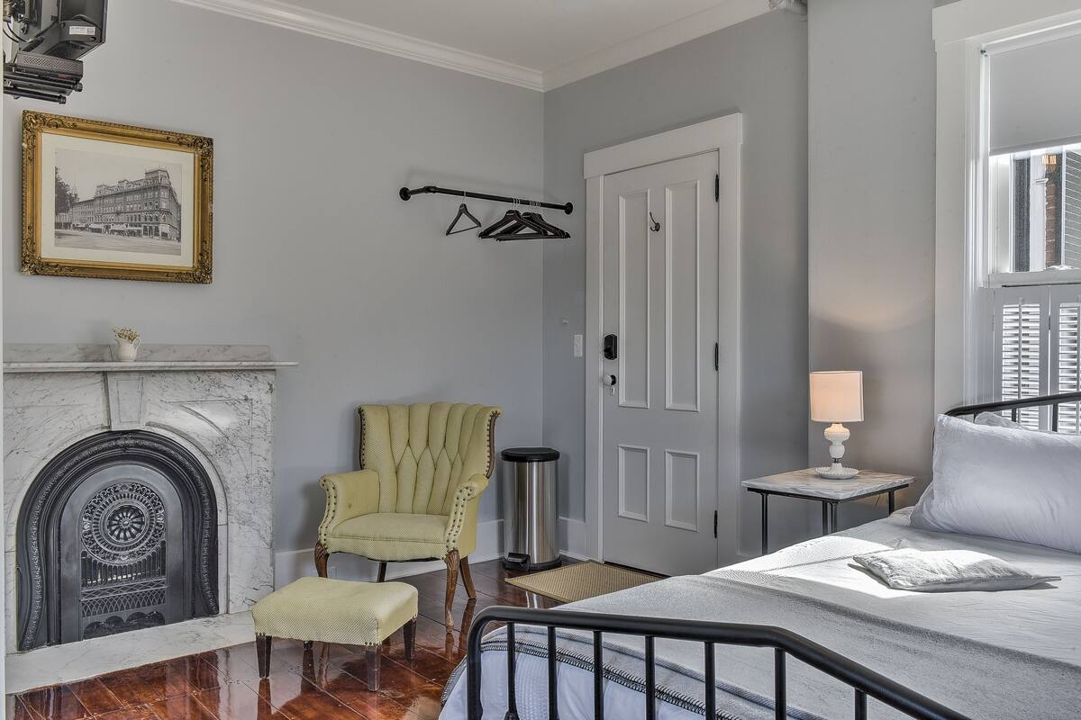 Quarto com cama, cadeira, lareira, porta e abajur.