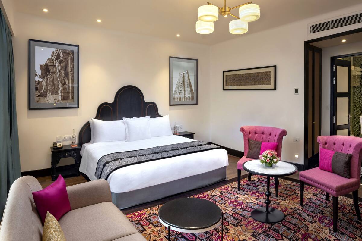 Quarto de hotel com uma cama, duas poltronas, uma mesinha e obras de arte nas paredes.