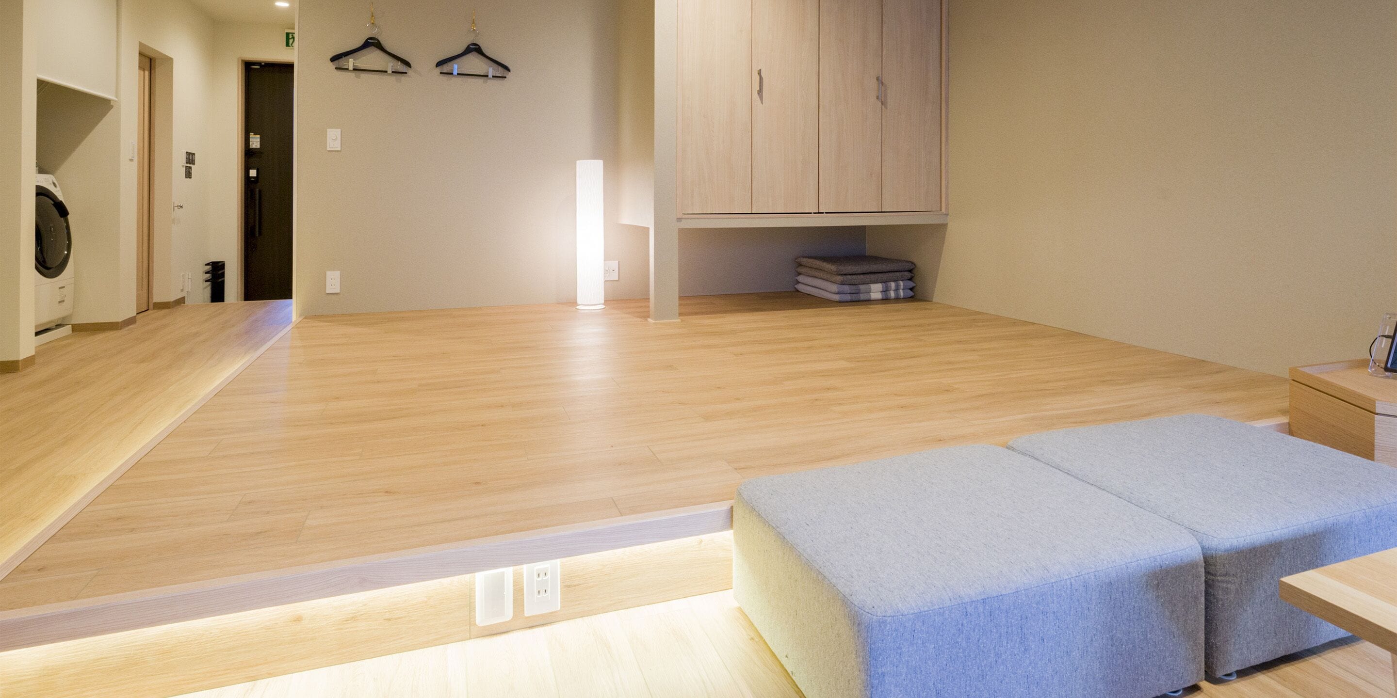 Um quarto amplo com piso de madeira, um banco acolchoado cinza e um guarda-roupa.