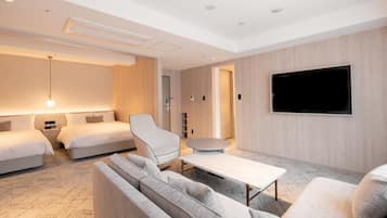 Quarto de hotel moderno com uma cama grande, um sofá, uma mesa de centro e uma televisão de tela plana fixada na parede.