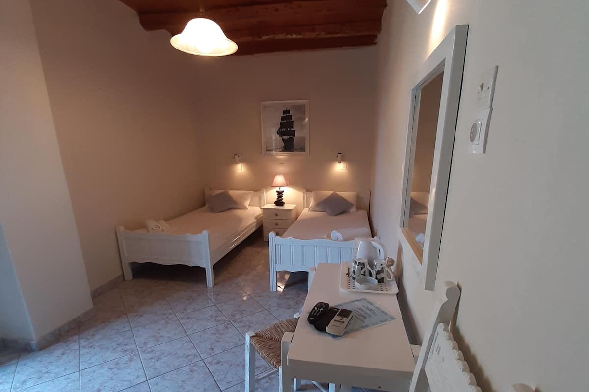 Um quarto aconchegante com duas camas, uma mesa de jantar e uma cadeira. Há uma lâmpada sobre a mesa e um quadro na parede.