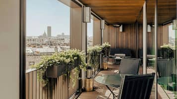 Uma varanda moderna com teto de madeira, guarda-corpos de vidro e vista para a cidade.