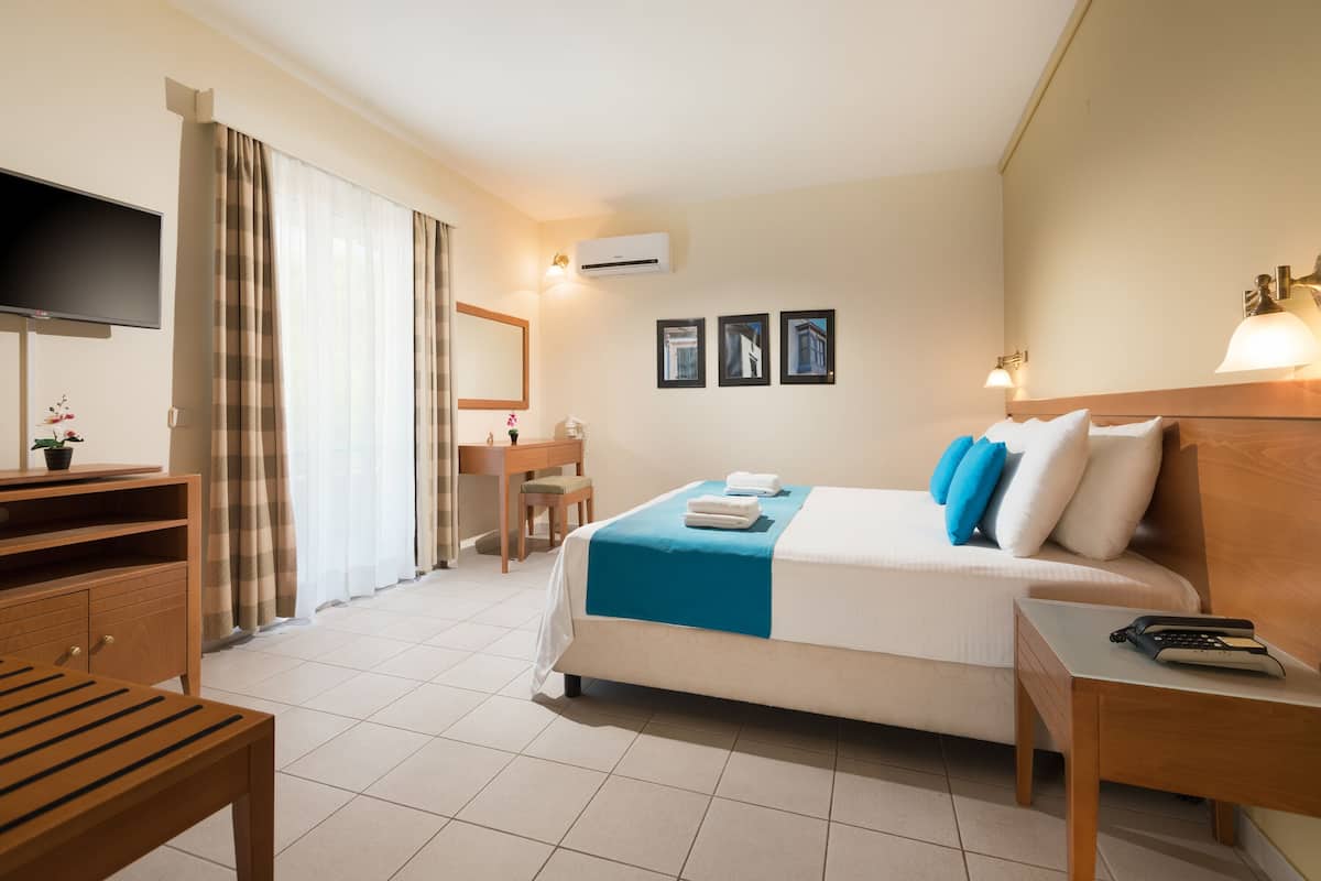 Quarto de hotel com cama, escrivaninha, televisão e janela com cortinas.