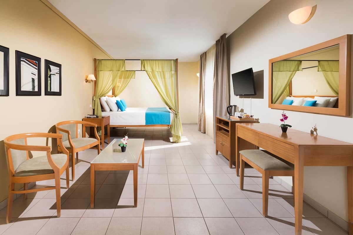 Quarto de hotel com cama, escrivaninha, cadeira, televisão e janela com cortinas.