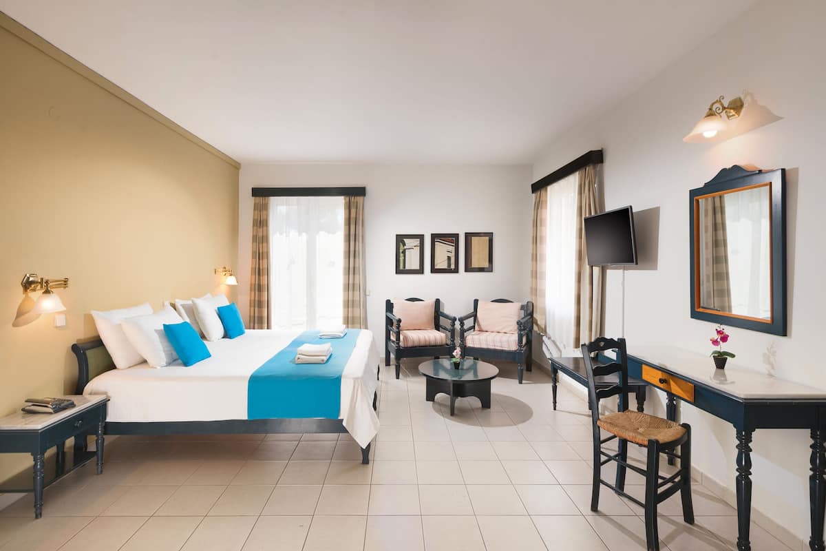 Quarto de hotel com cama, escrivaninha, cadeira, televisão e janela com cortinas.
