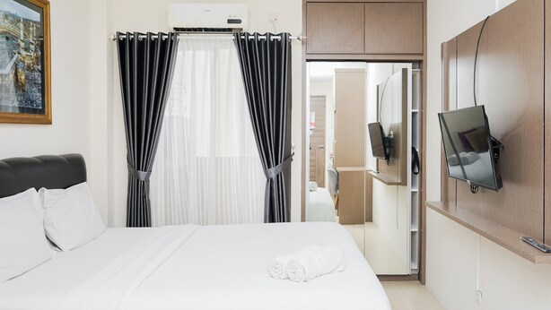 Quarto de hotel com uma cama, uma TV fixada na parede e uma porta para o banheiro.