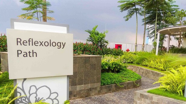 Placa com a inscrição 'Reflexology Path' em área ajardinada com vegetação e um caminho.