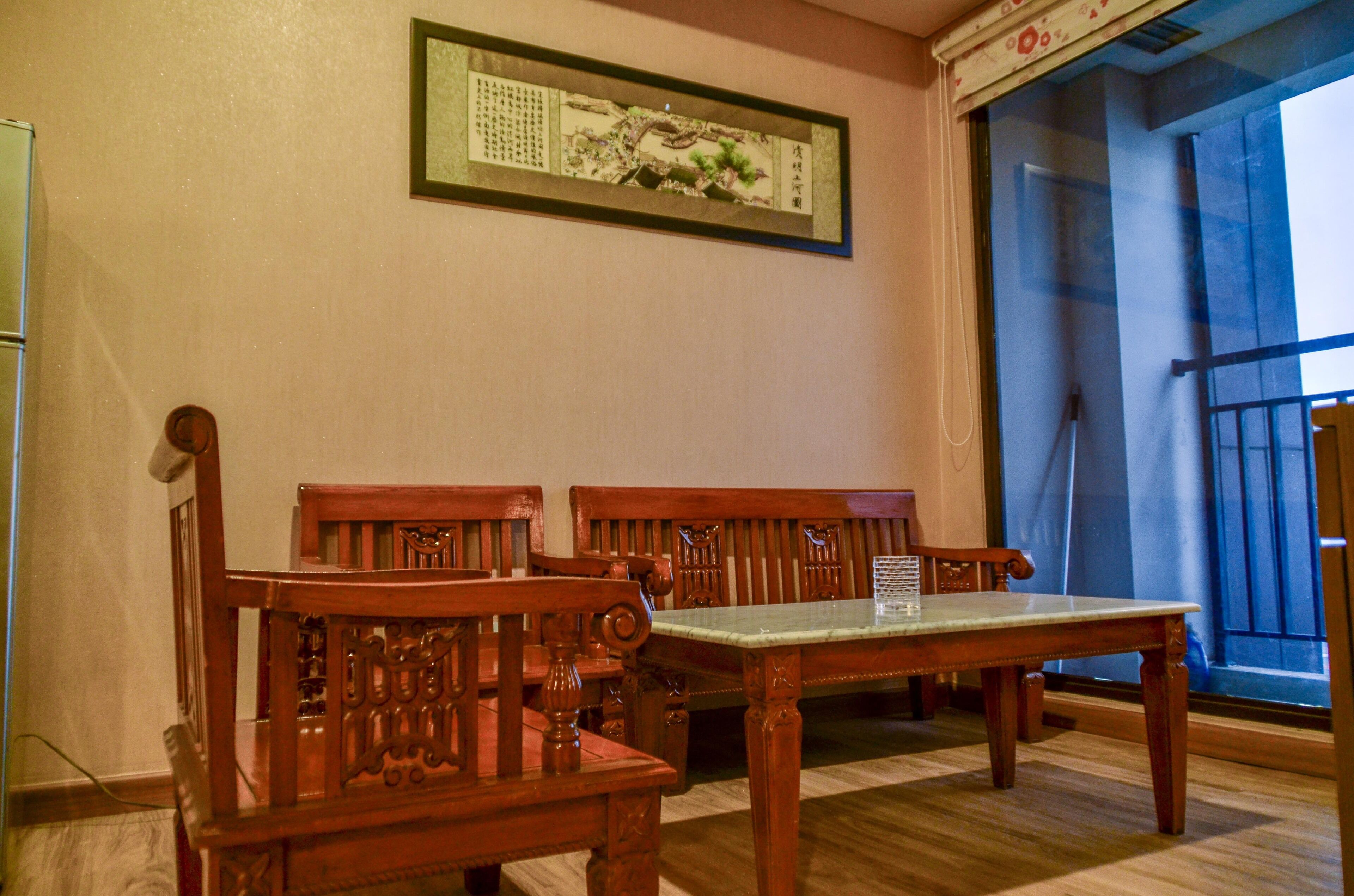 Uma área de refeições com mesa e bancos de madeira, uma obra de arte emoldurada na parede e vista para o exterior pela janela.