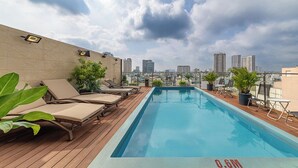Piscina no terraço com espreguiçadeiras e plantas em vasos, com vista para a cidade.